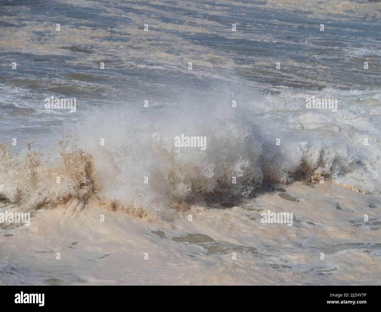 Frothy ocean waves crashing into the beach sand, breaking near the ...