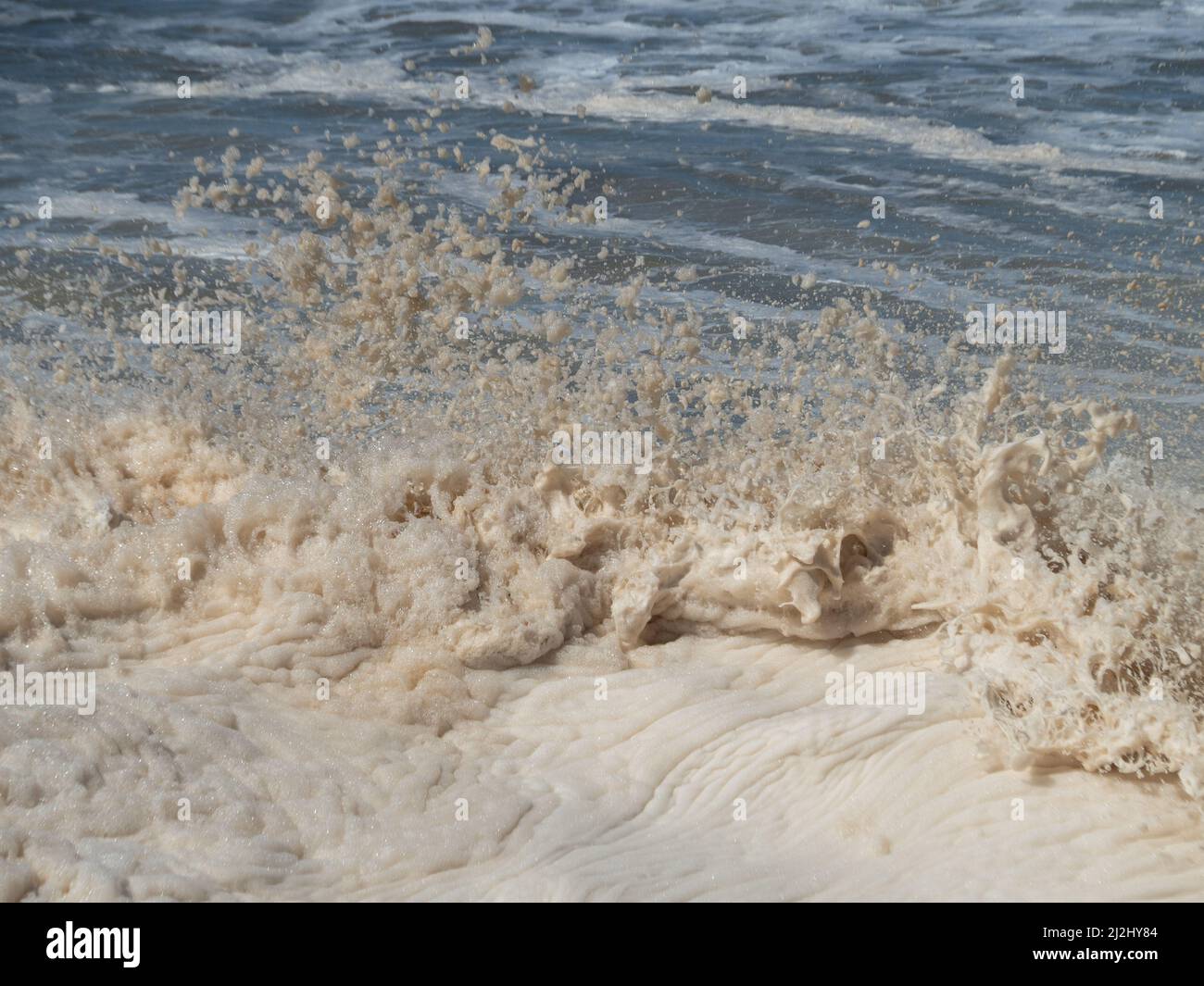 Frothy ocean waves mixing with the sand on the beach, breaking near the ...