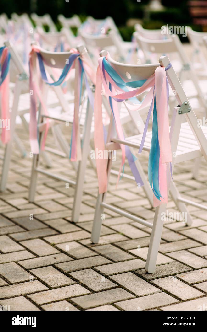 White wooden chairs decorated with pink and blue ribbons. Wedding ...