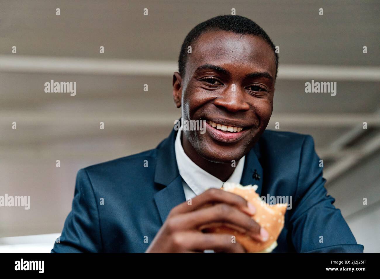 Young african american man eating a tasty classic burger looking at the ...