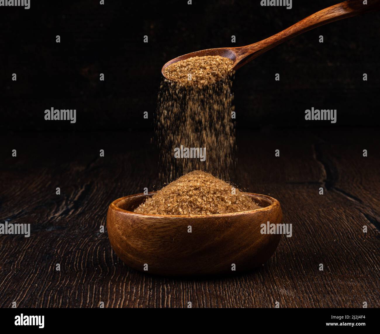 Cane sugar is poured from a spoon into a pile of sugar in a wooden bowl ...