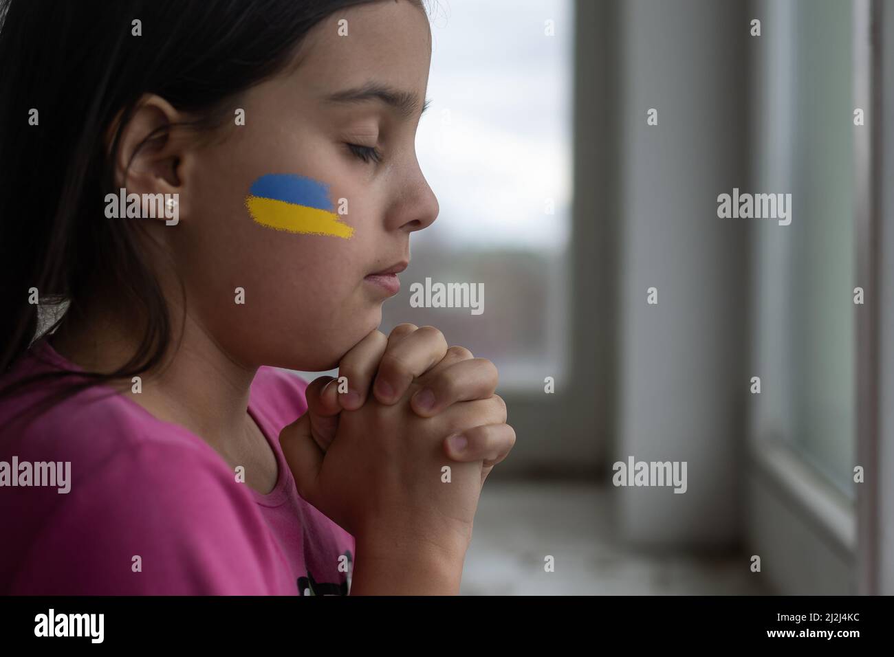 Little girl with Ukrainian flag ribbon praying. Symbol of peace and ...