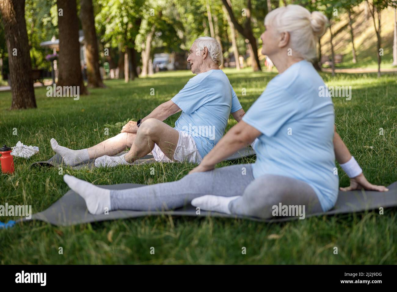 Senior family couple does yoga exercises sitting on lush lawn in ...