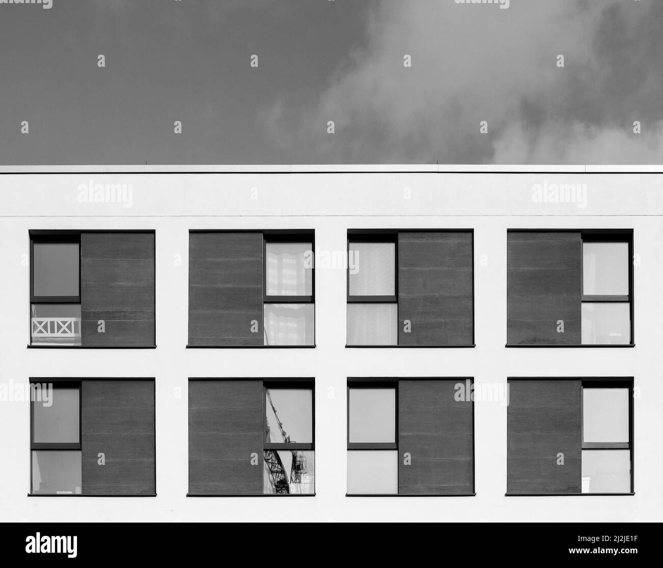 A grayscale shot of the windows in a modern building under cloudy sky ...