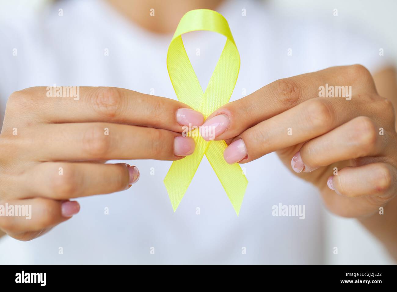 Yellow ribbon in hands, symbol Bladder cancer Stock Photo - Alamy