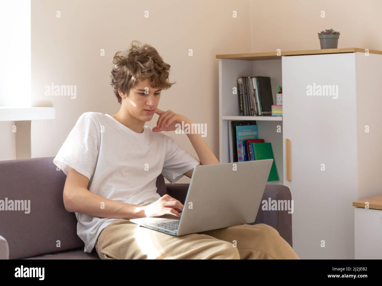 Cute young teenager with laptop on the couch at home. Boy makes ...