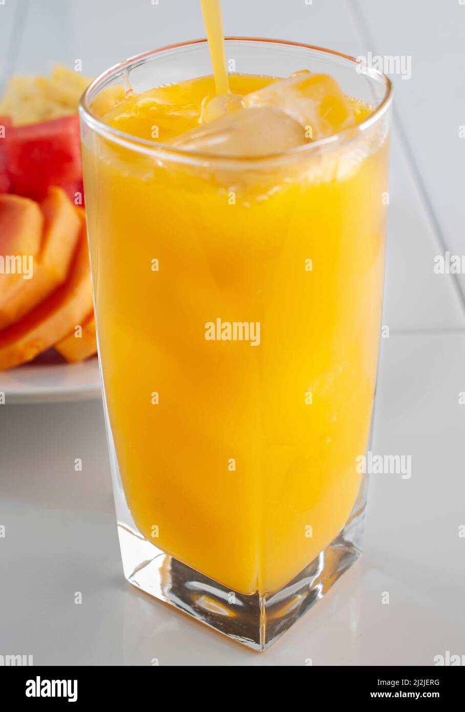 A mango juice in a sqaure shaped glass with ice, on a white kitchen ...