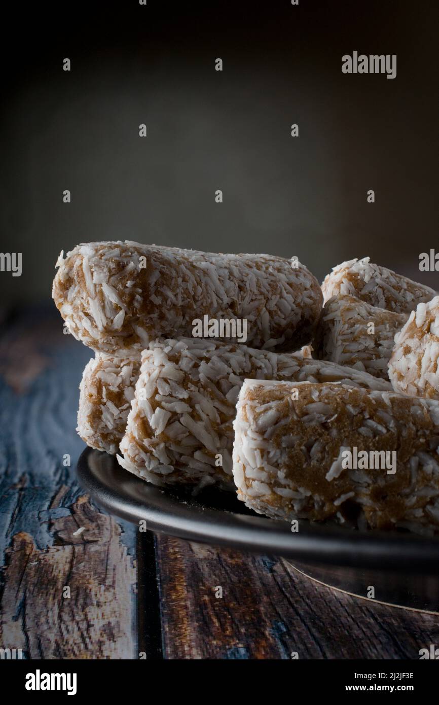 Candies, rolls of dates covered with coconut flakes on a black plate ...