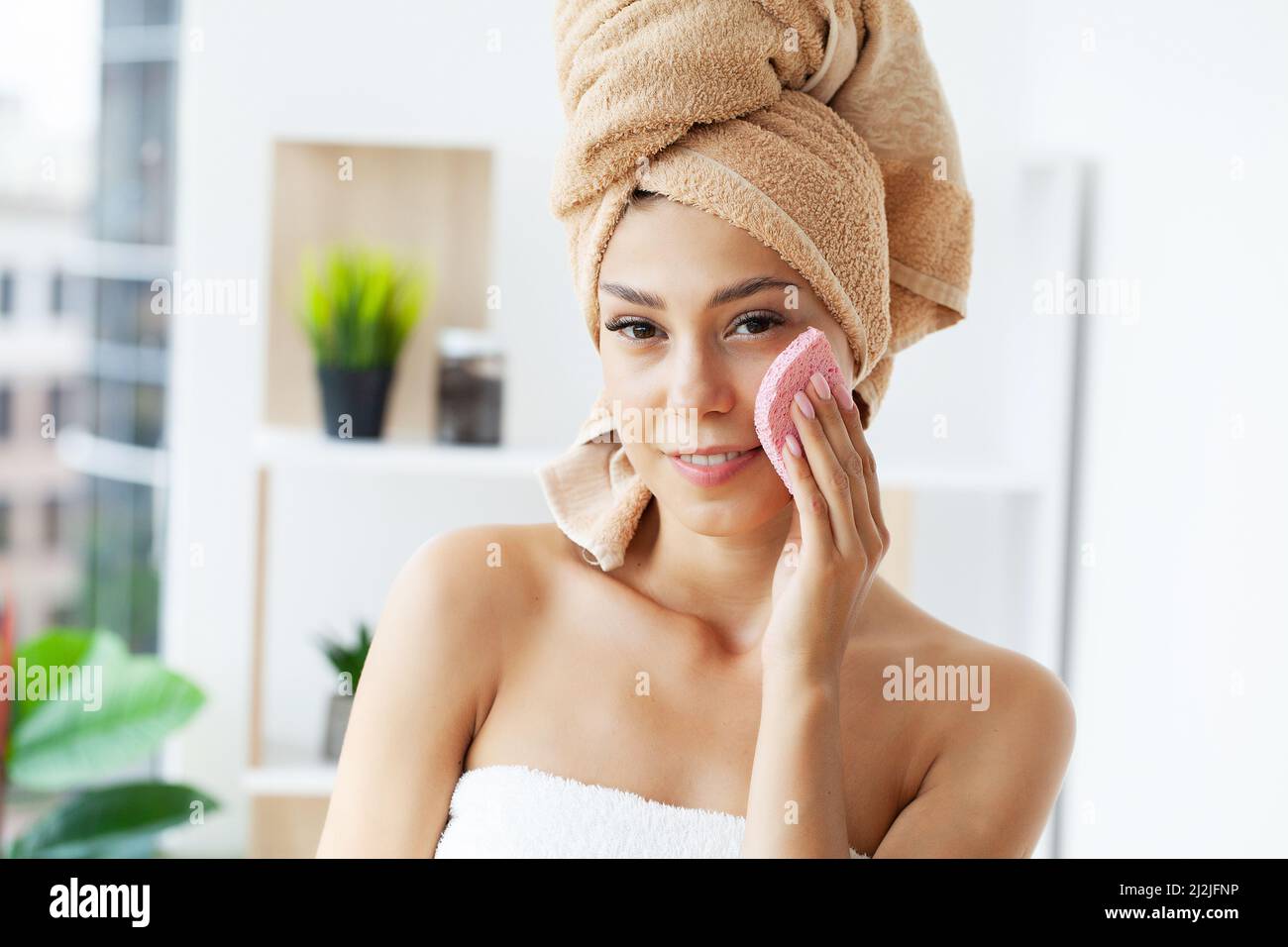Young happy woman in towel making facial massage with organic face scrub in stylish bathroom ...