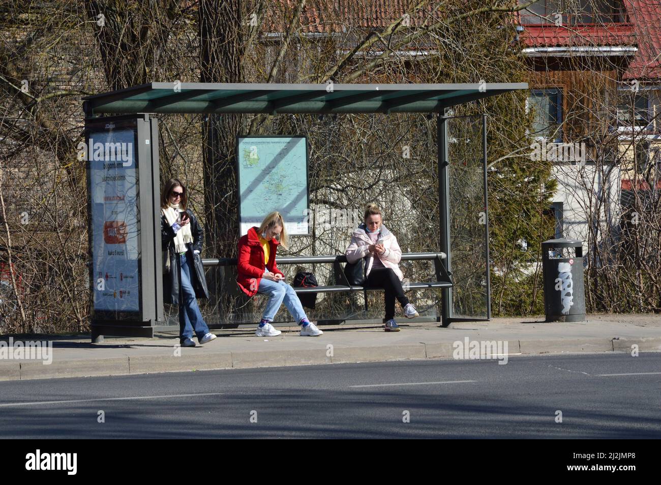 Three young women using smartphones at a bus stop in the Old Town of ...