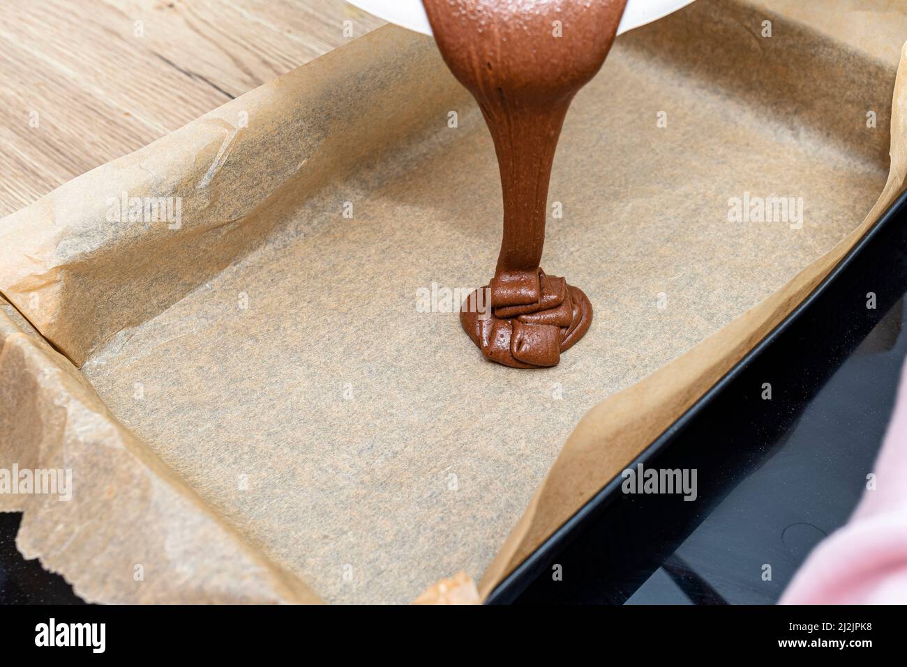Pouring a liquid thick mass of cocoa dough onto a baking sheet lined ...
