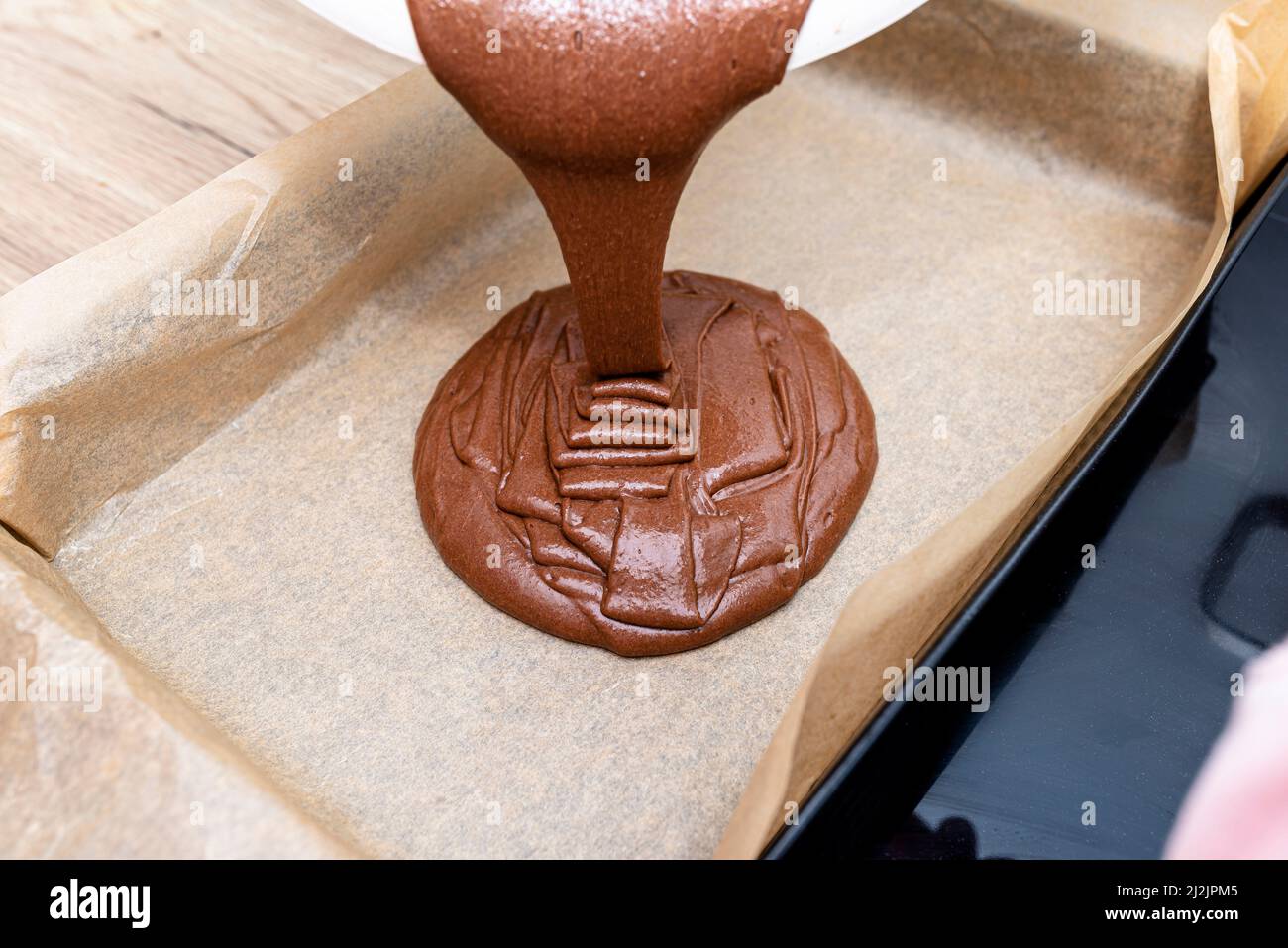 Pouring a liquid thick mass of cocoa dough onto a baking sheet lined ...