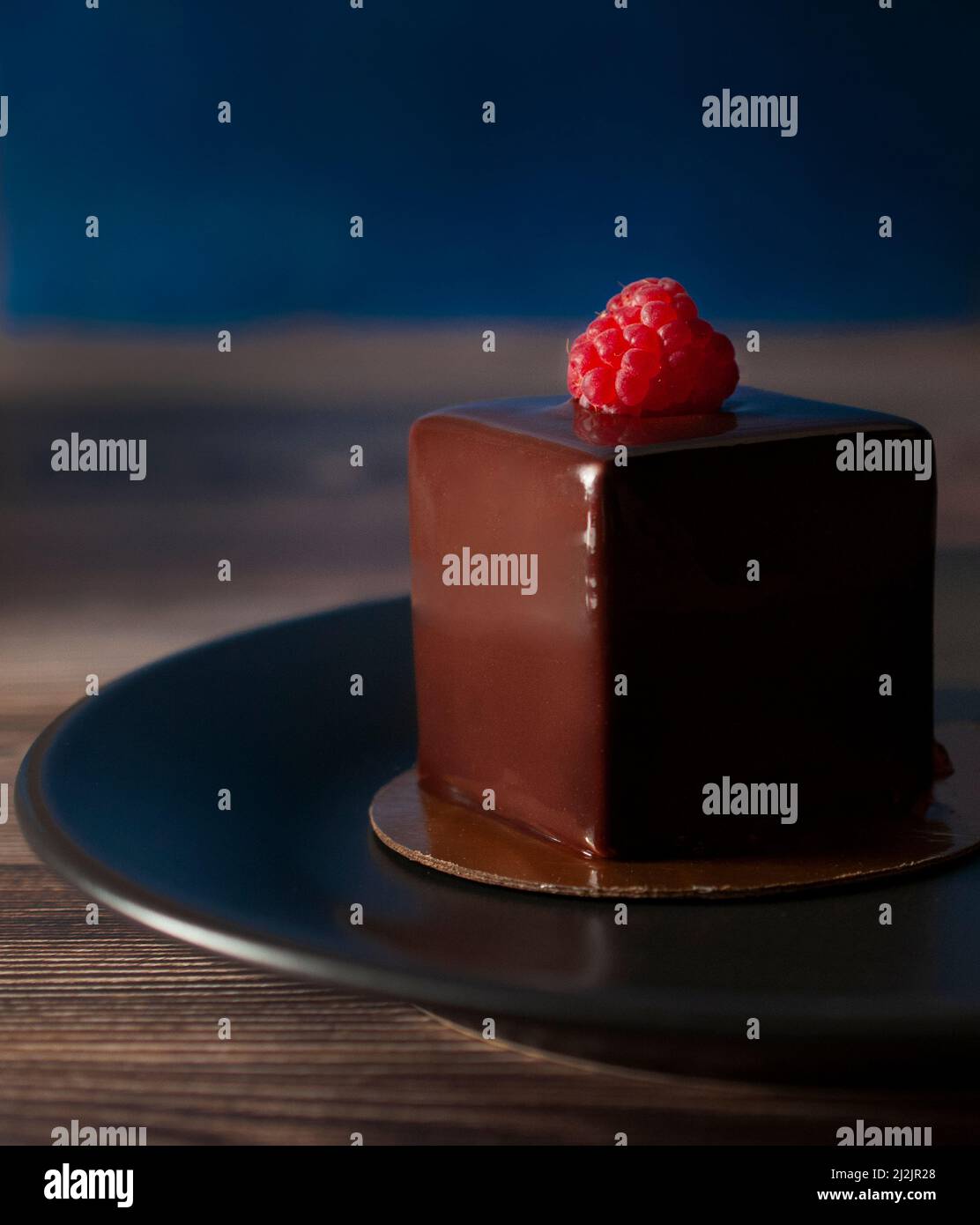 French fine chocolate pastry in the shape of a cube with a raspberry on ...