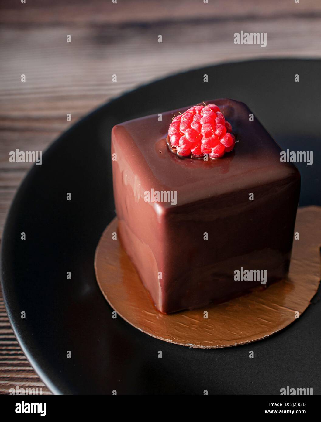 French fine chocolate pastry in the shape of a cube with a raspberry on ...