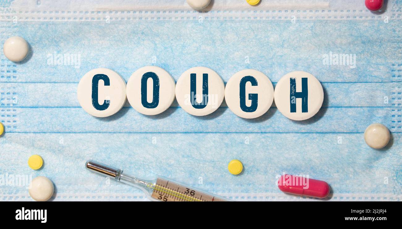 the word COUGH on wooden cubes on grey background with a jar of pills ...