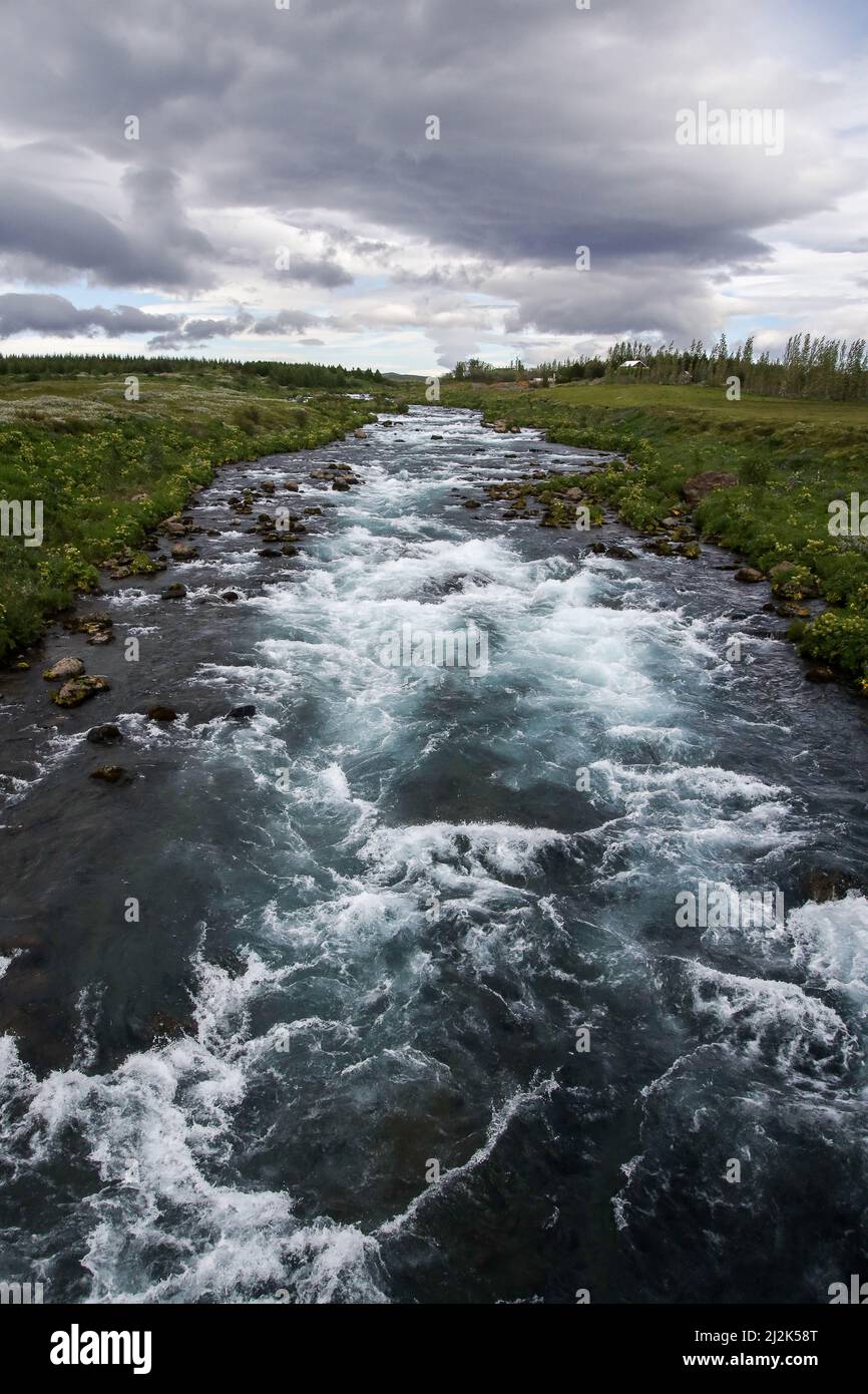 A vertical shot of a river flowing through its banks partly covered ...