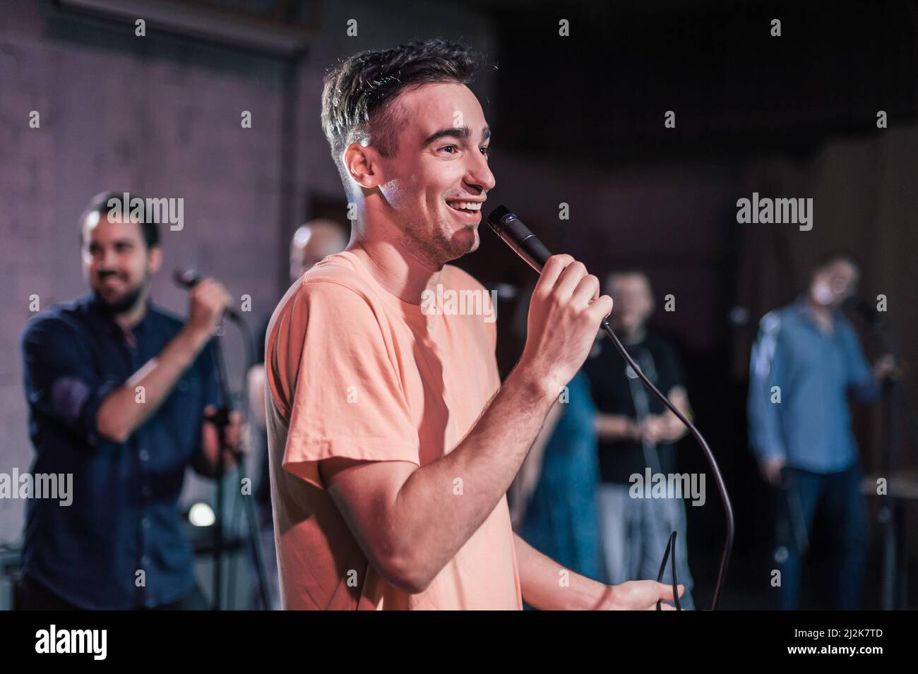 Smiling and witty stand up actor comedian on stage, talking and singing ...