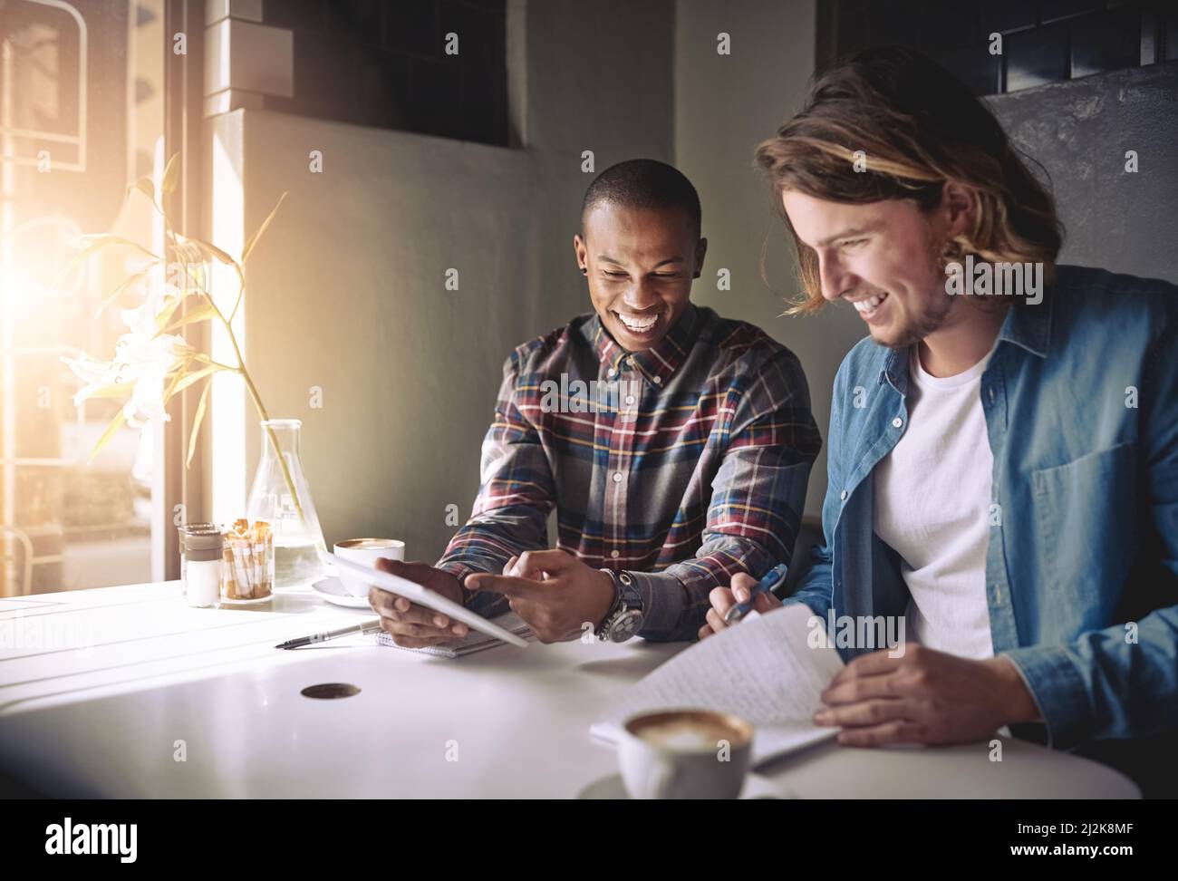 Coffee fuels their creativity. Shot of two friends using a tablet while ...
