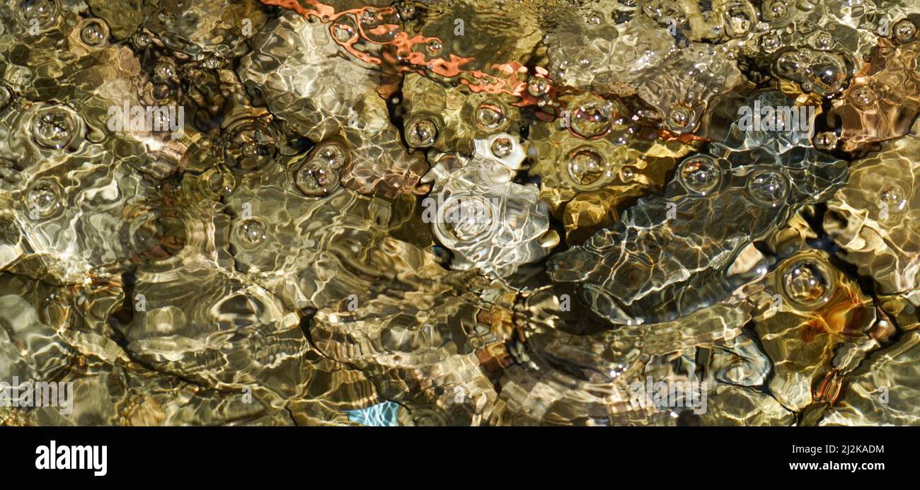 A top view of crystal clear transparent water of a lake with rocks on ...