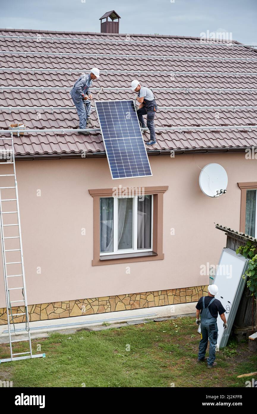 Men technicians lifting up photovoltaic solar modul on roof of house ...