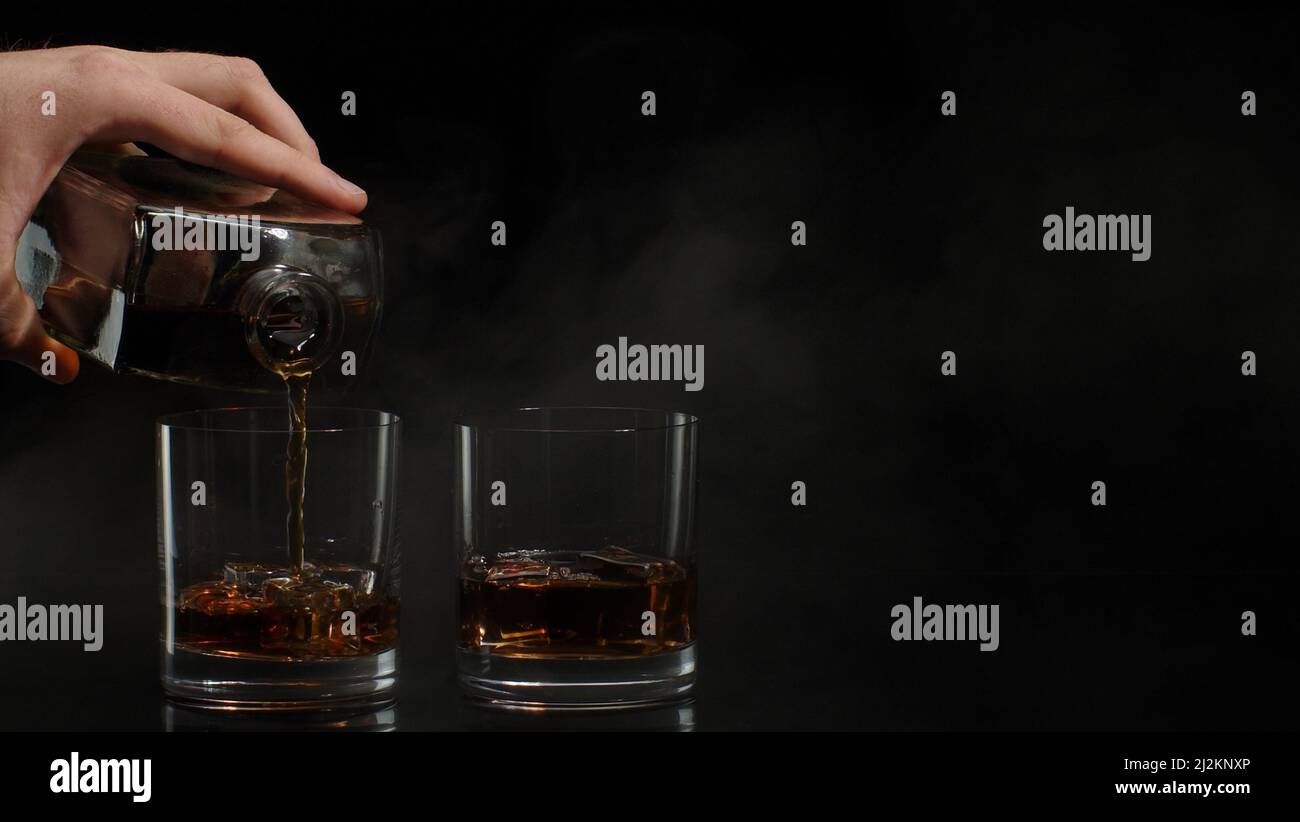 Barman pour golden whiskey cognac brandy from bottle into glasses with ...
