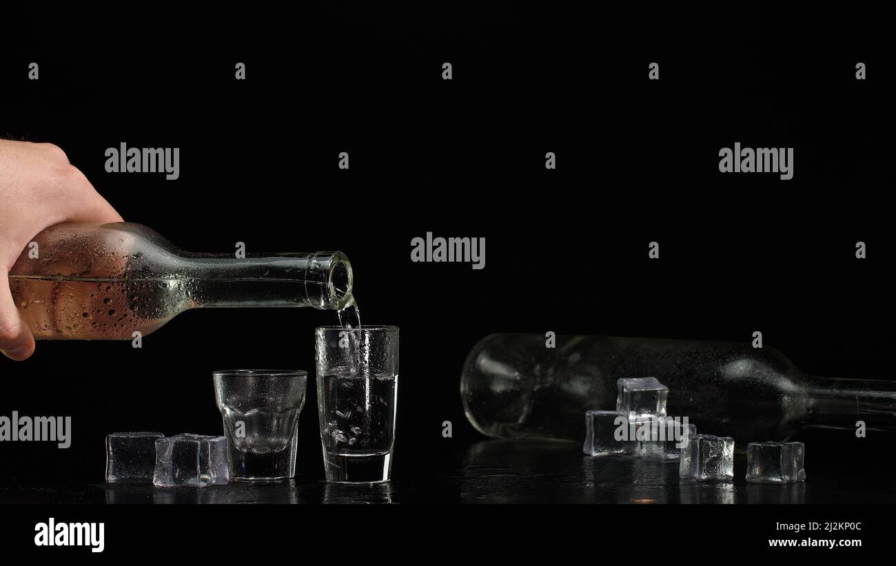 Bartender pouring up two shots of vodka with ice cubes from bottle into ...