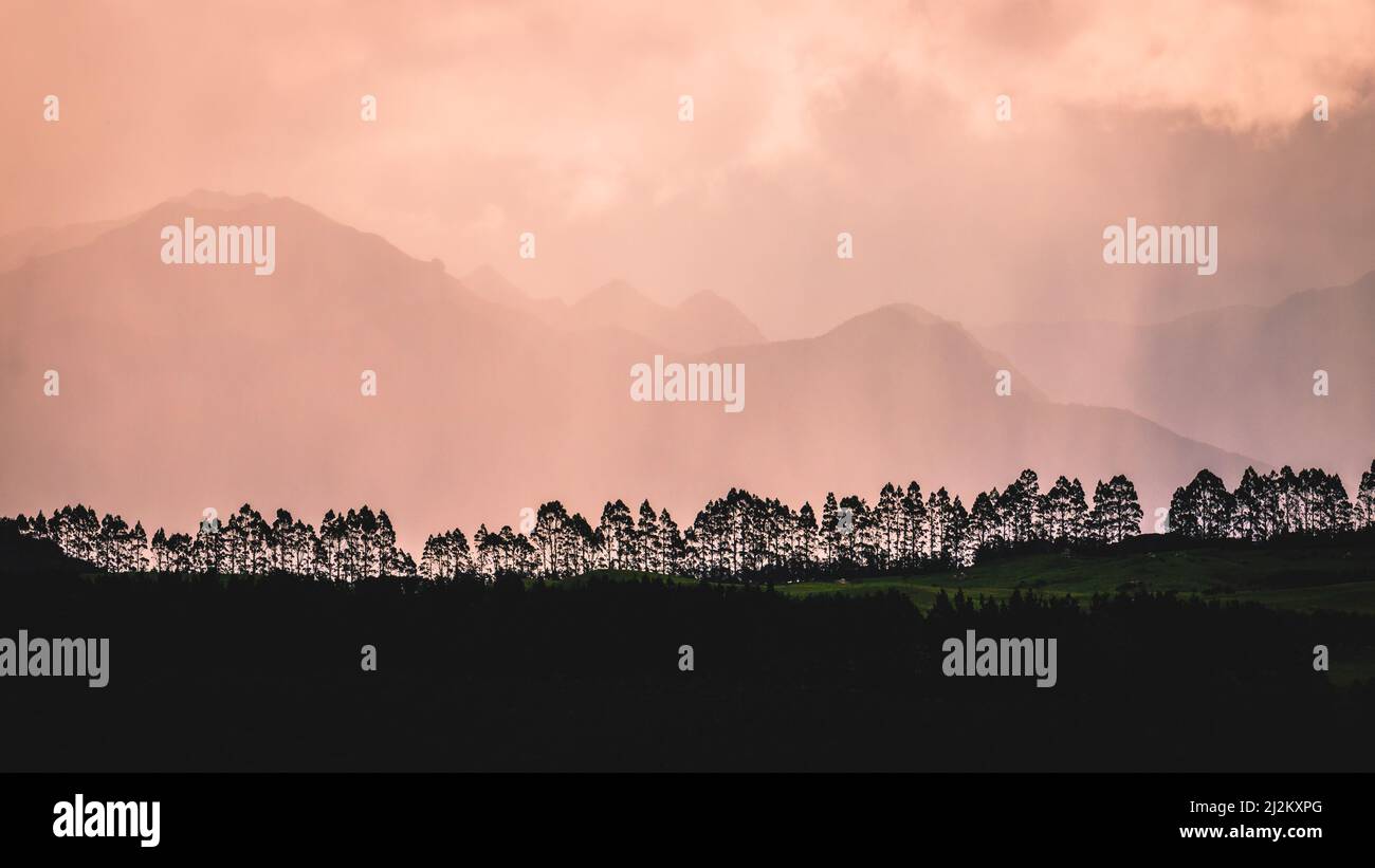 A hazy red view of hills and mountains with a silhouette of a row of ...