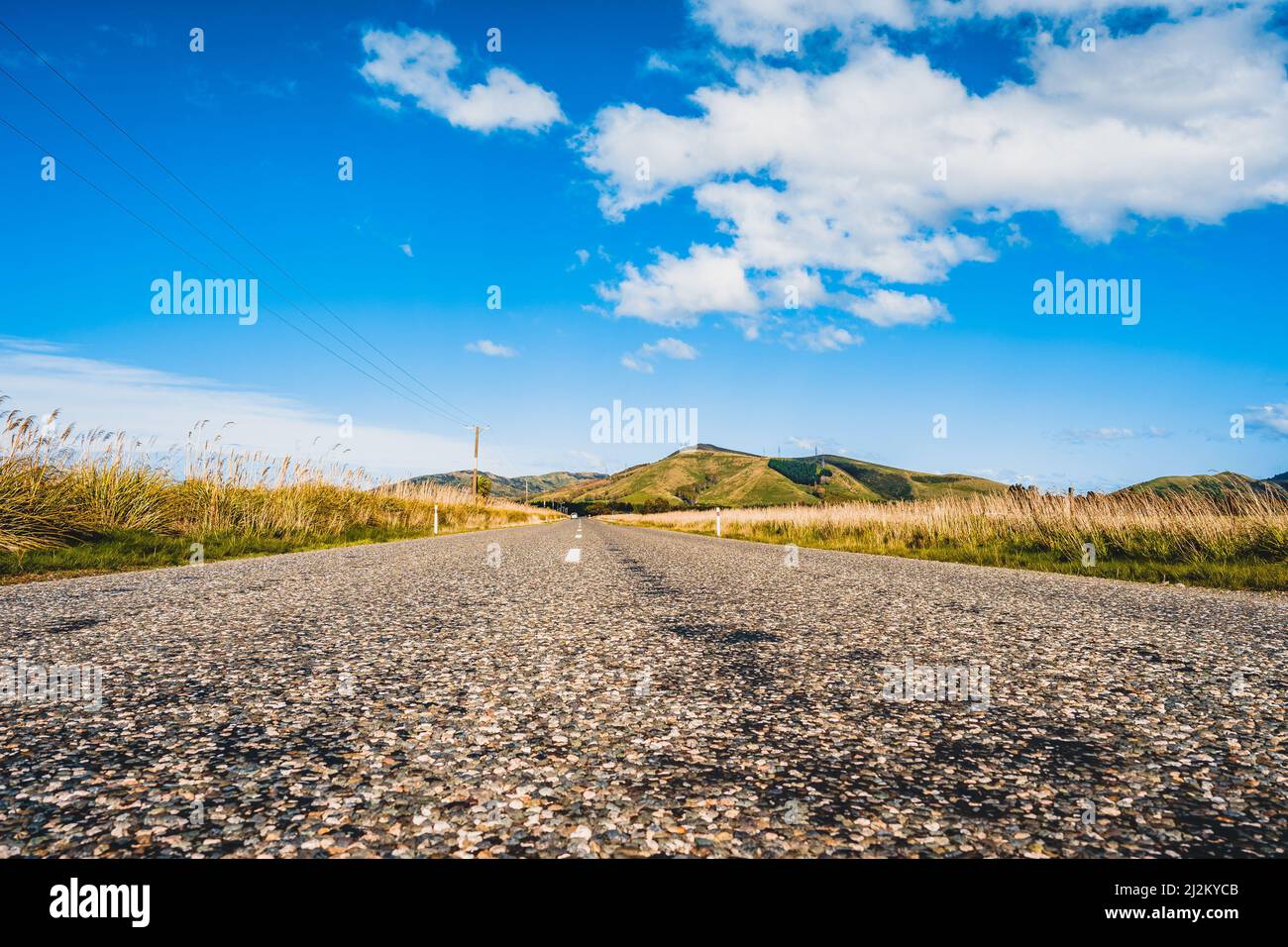 A view of a paved road, meadows and hills on a sunny day with blue ...