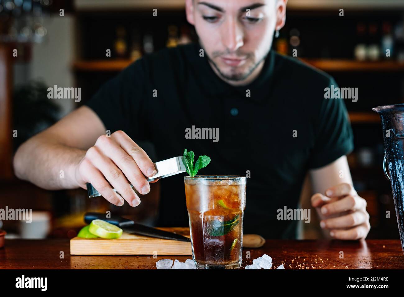 Young waiter, putting mint leaves to decorate a cocktail. Horizontal ...