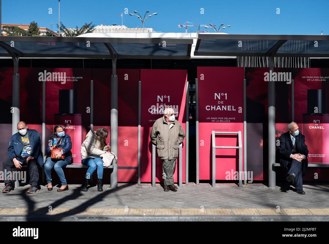 Commuters wait at a bus stop decorated with a commercial advertisement ...