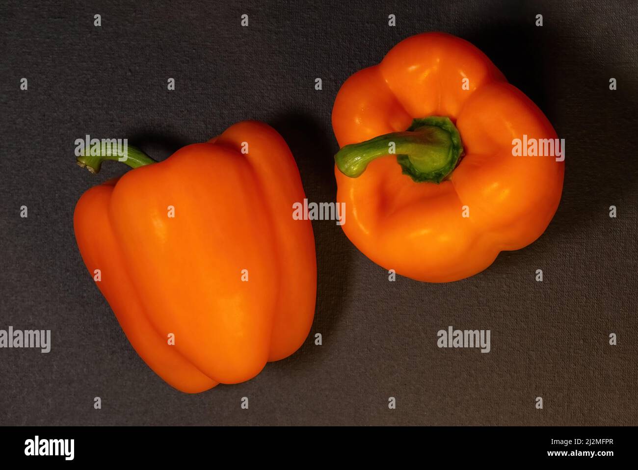 Two ripe orange bell peppers on a dark background, whole vegetables ...