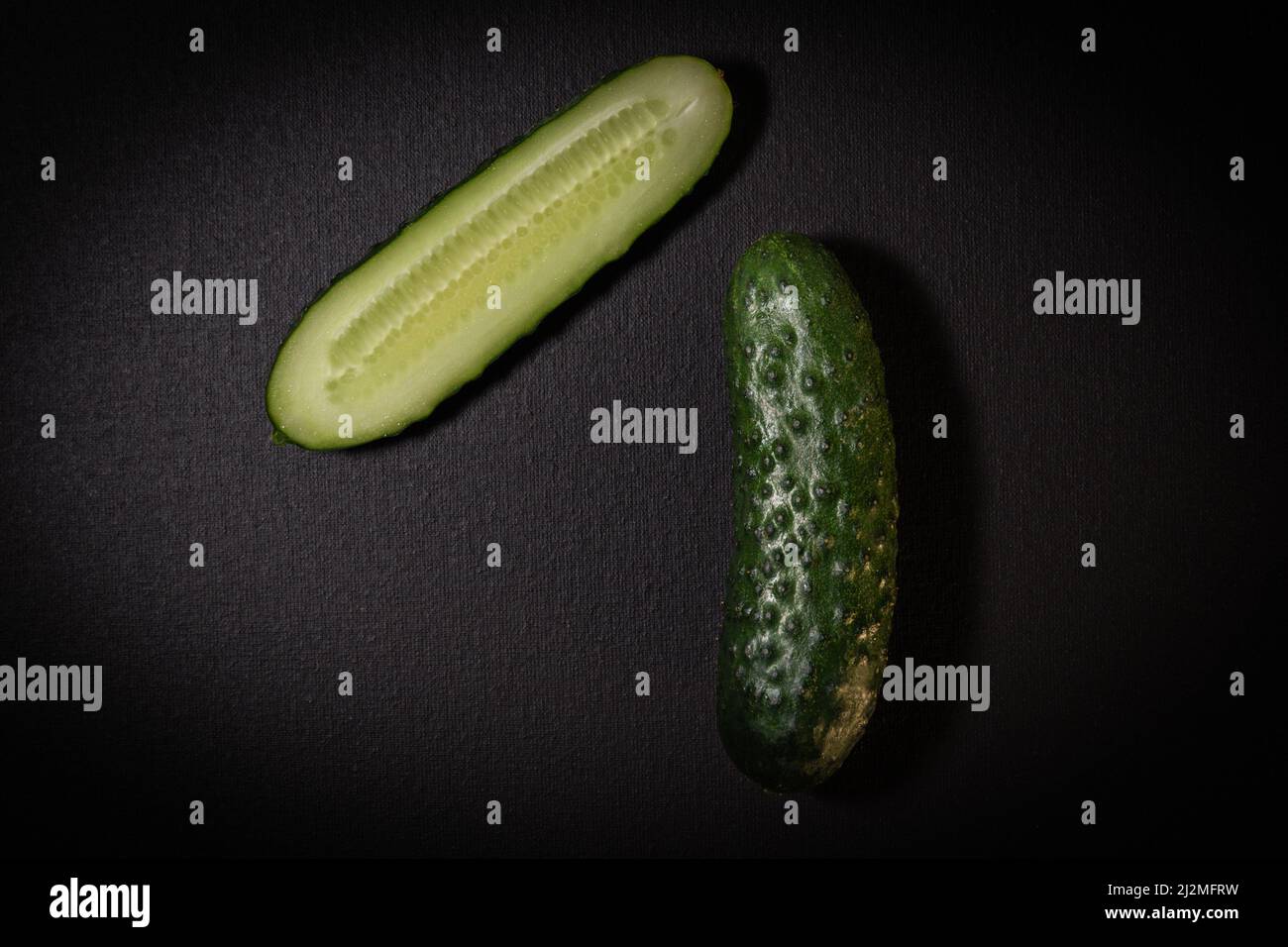 Two green cucumbers on a dark background. Whole cucumber and cut in ...
