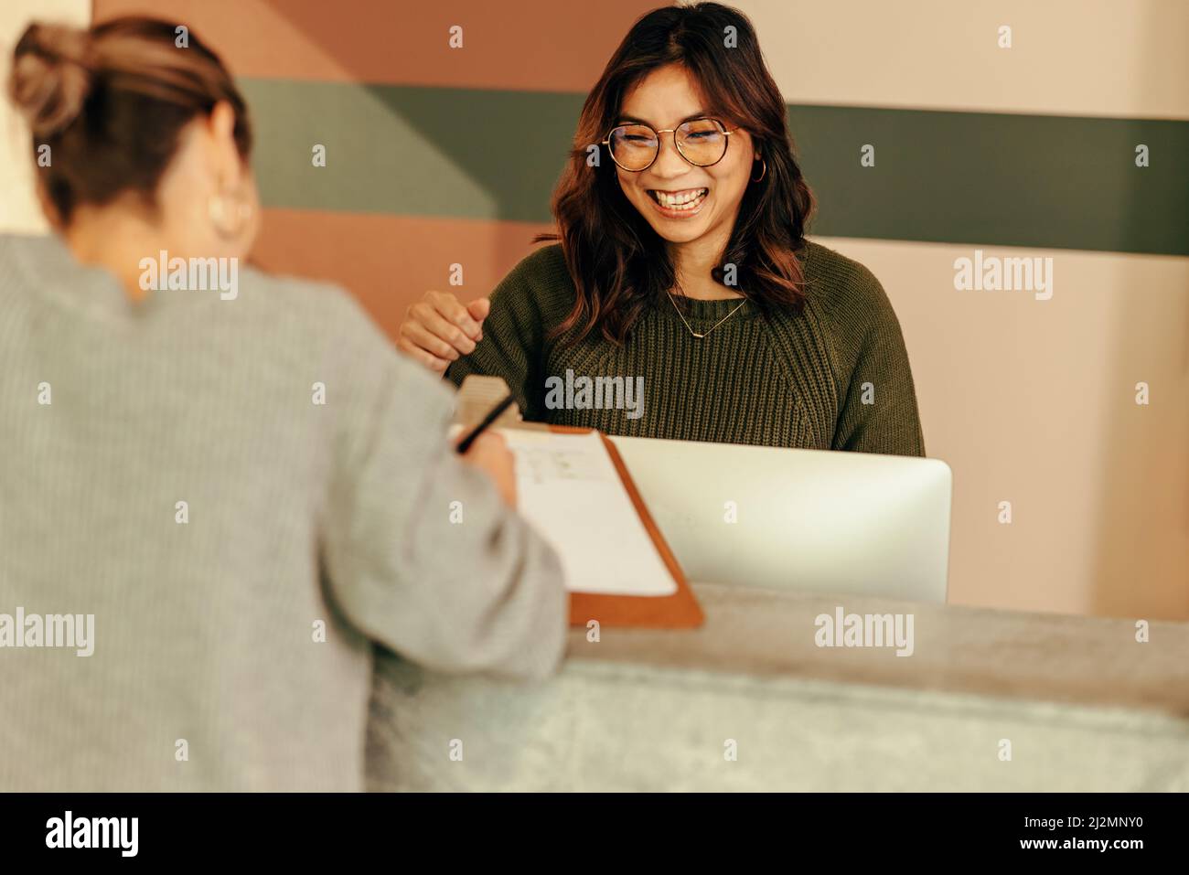 Cheerful receptionist assisting a woman with signing in to an office ...