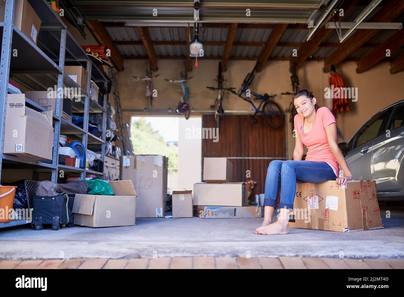 Sitting amongst the storage. Portrait of a young girl sitting on a box ...