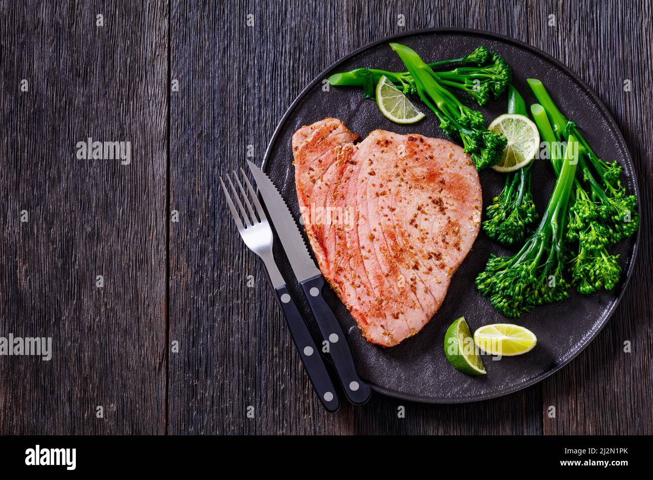 fried tuna steak with parboiled broccolini and lime on black plate on ...