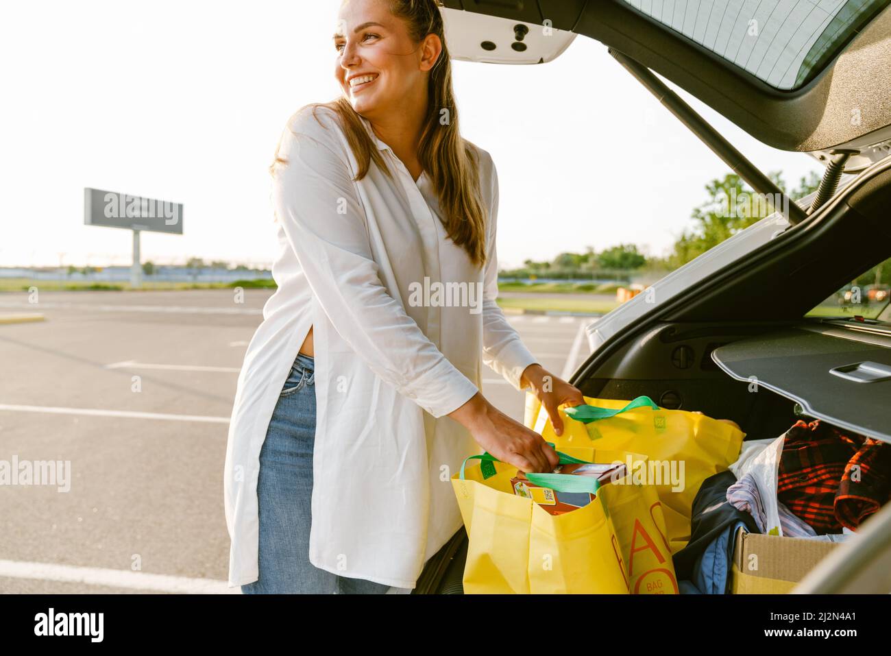 White woman smiling while getting shopping bag out of trunk at parking ...