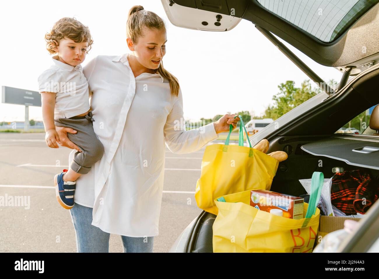 White woman holding her son while getting shopping bag out of trunk at ...
