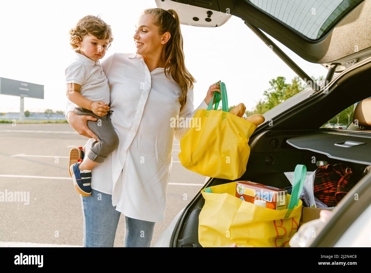 White woman holding her son while getting shopping bag out of trunk at ...