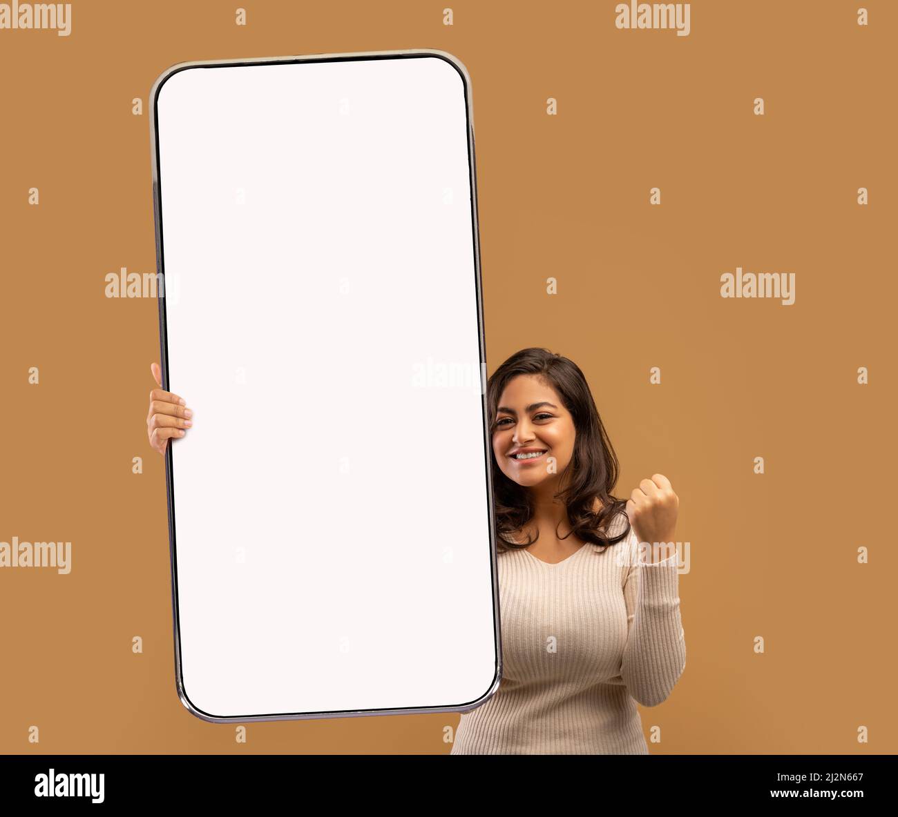Attractive young Arab woman gesturing YES, holding big cellphone with ...