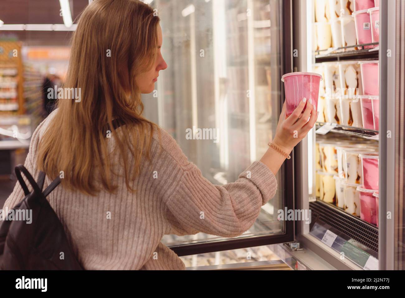 Woman buying bucket of strawberry ice cream from the fridge in the ...