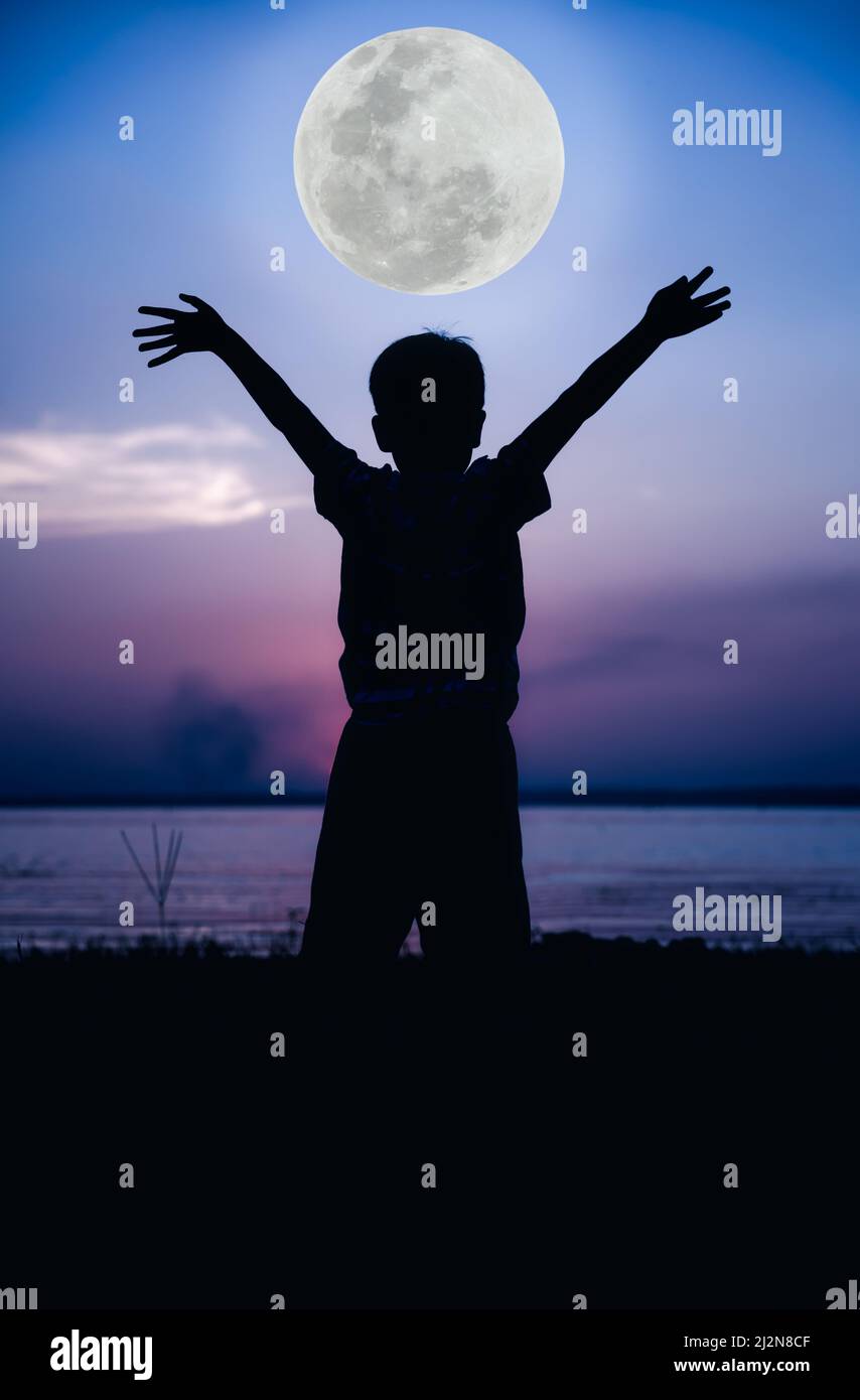 Silhouette back view of child enjoying the view at riverside. Full moon ...