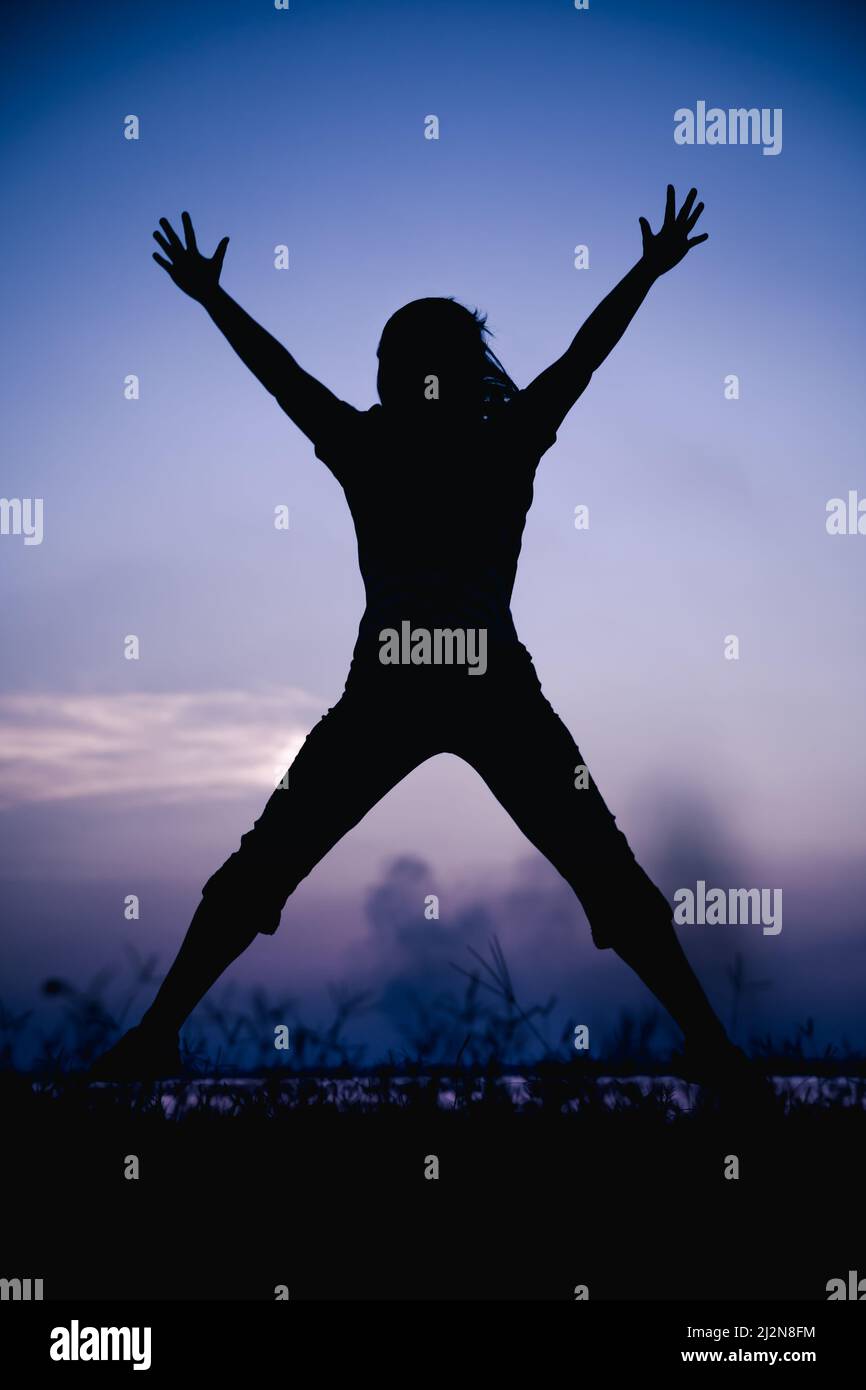 Silhouette back view of woman enjoying and jumping at riverside ...