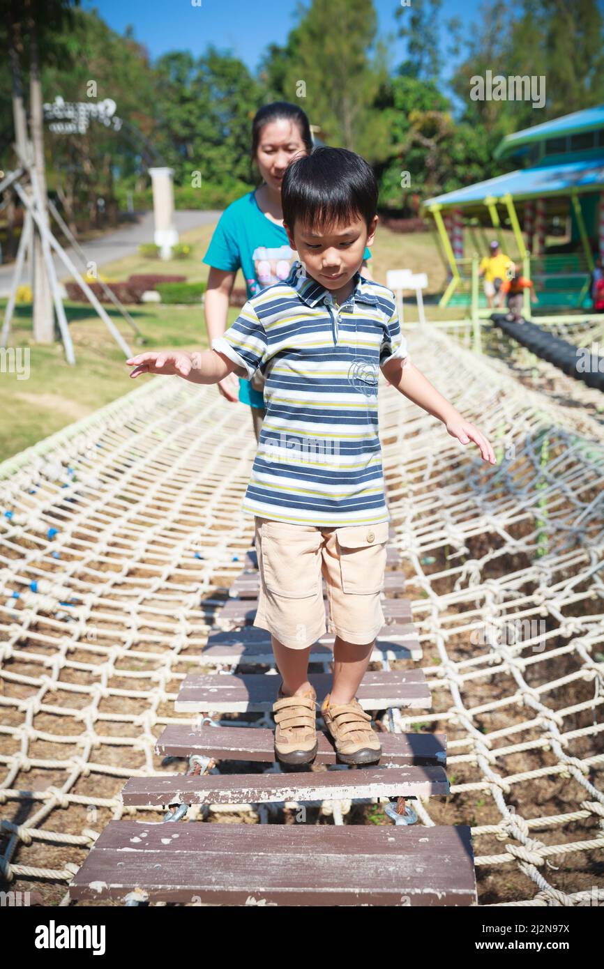 Cheerful child having fun at playground, mother near by. Boy playing at ...