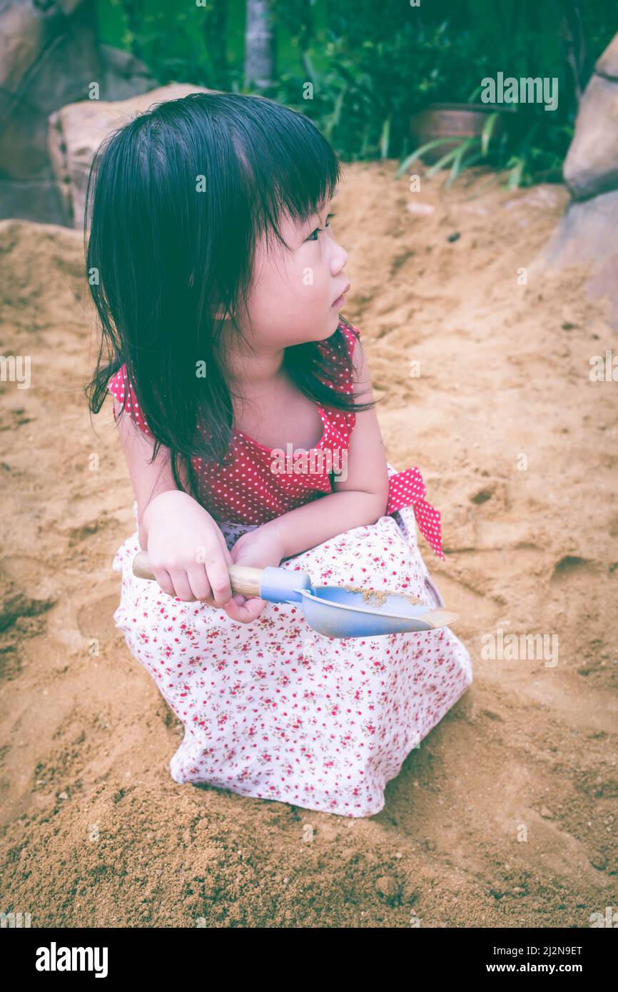 Happy child playing with sand. Adorable asian girl has fun digging in ...