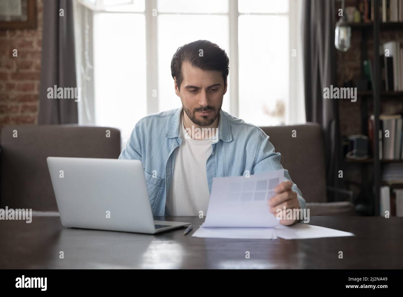 Focused professional interior designer reviewing paper with samples of ...