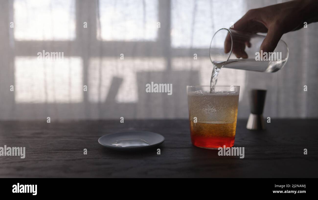 pour tonic water over ice ball with orange syrup in tumbler glass on ...