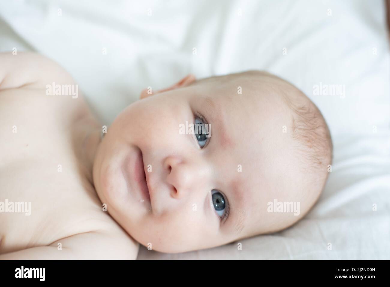 Adorable baby boy in white sunny bedroom. Newborn child relaxing in bed ...