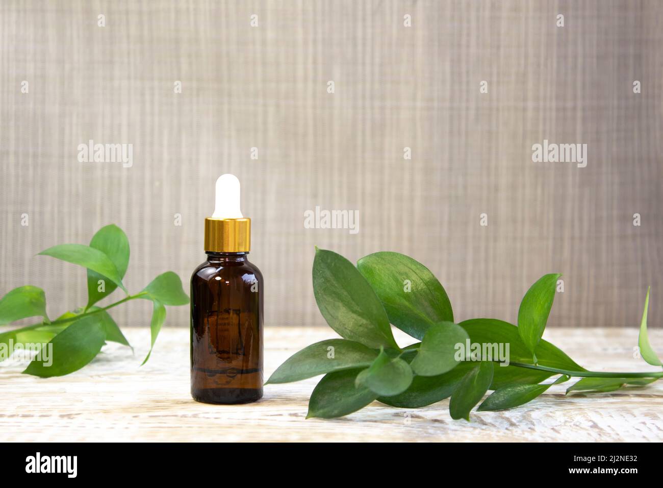 Brown jar with useful cosmetic oil and sprigs of a plant on blurred ...