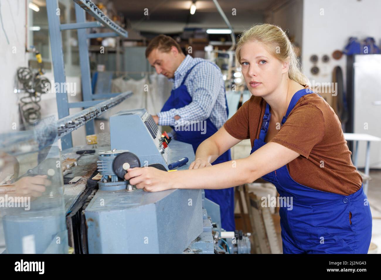 Female glazier with male colleague working on glass chamfering machine ...