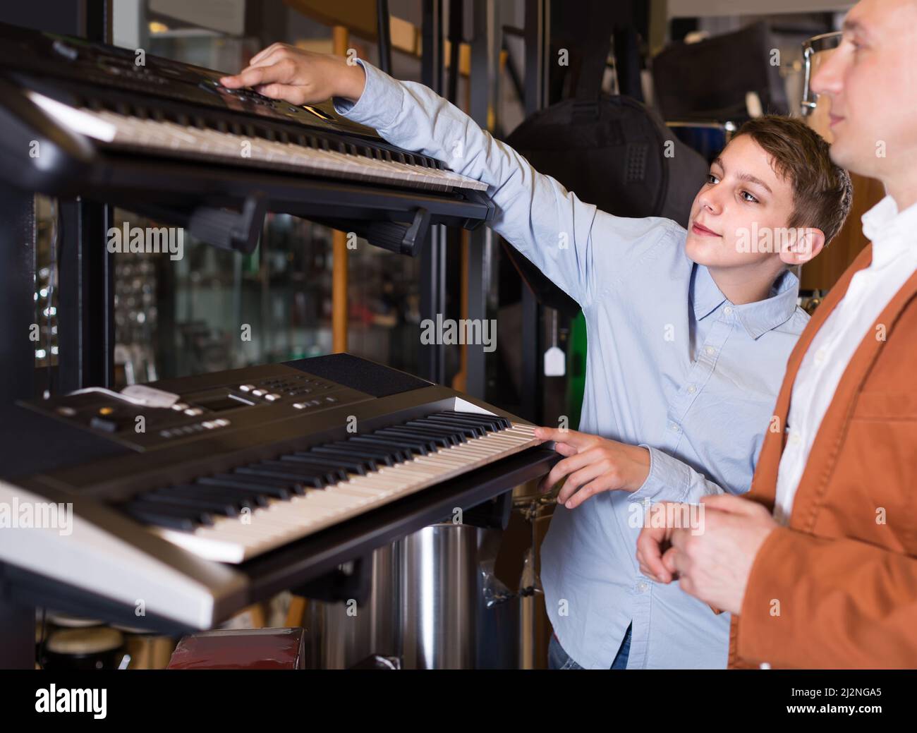Father and teenage son examining keyboards in guitar shop Stock Photo ...